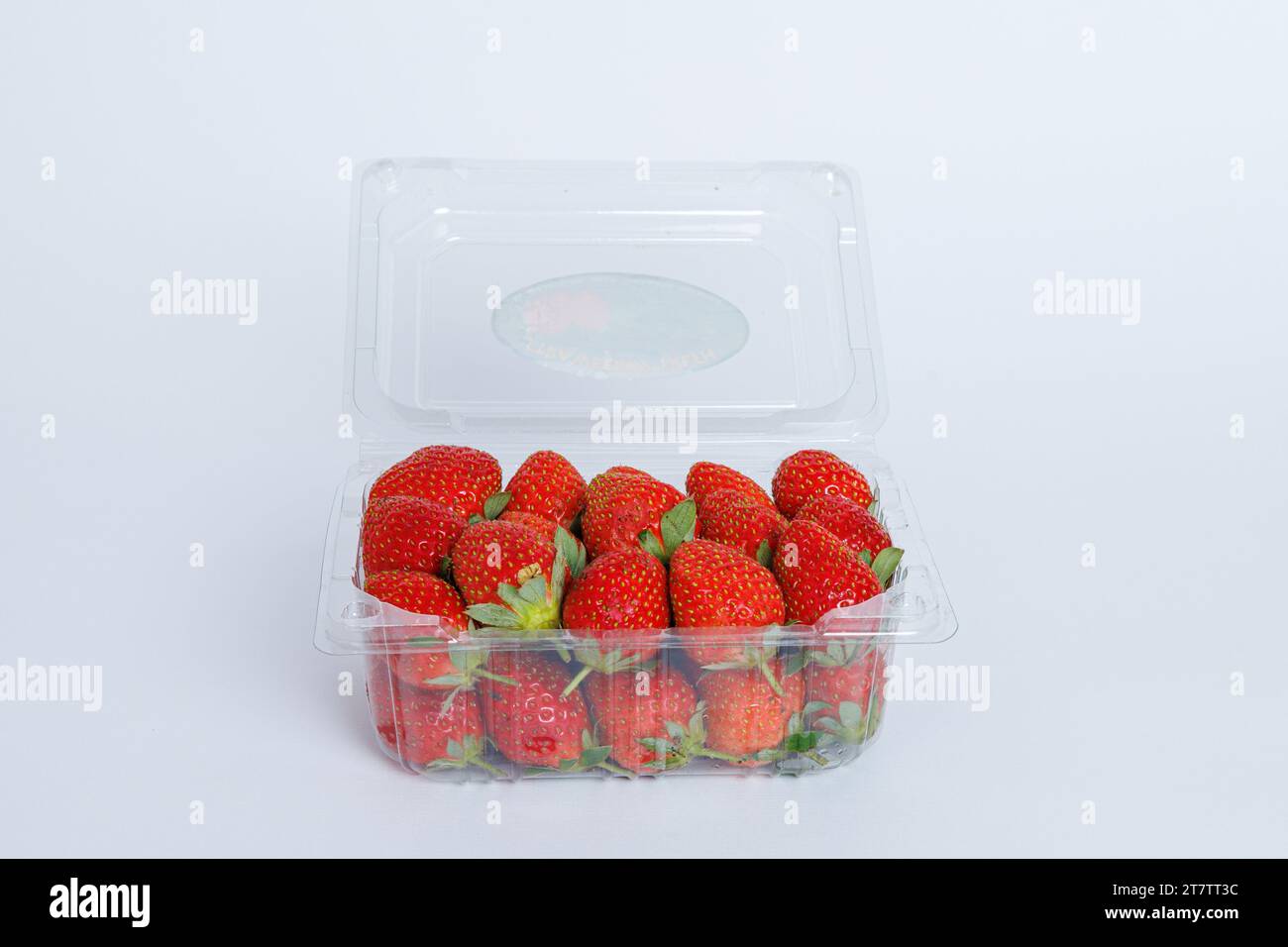 Red ripe strawberries with green stems in plastic tray container with ...