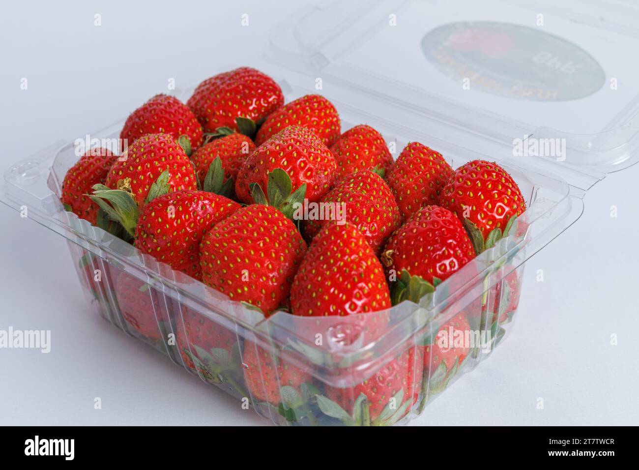 Red ripe strawberries with green stems in plastic tray container with ...