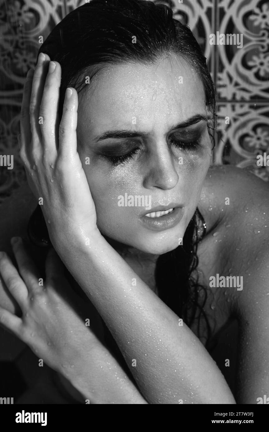 Sad and wet woman with smudged makeup on her face under the shower ...