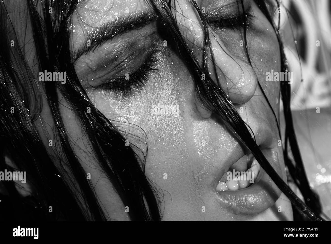 Sad and wet woman with smudged makeup on her face under the shower ...