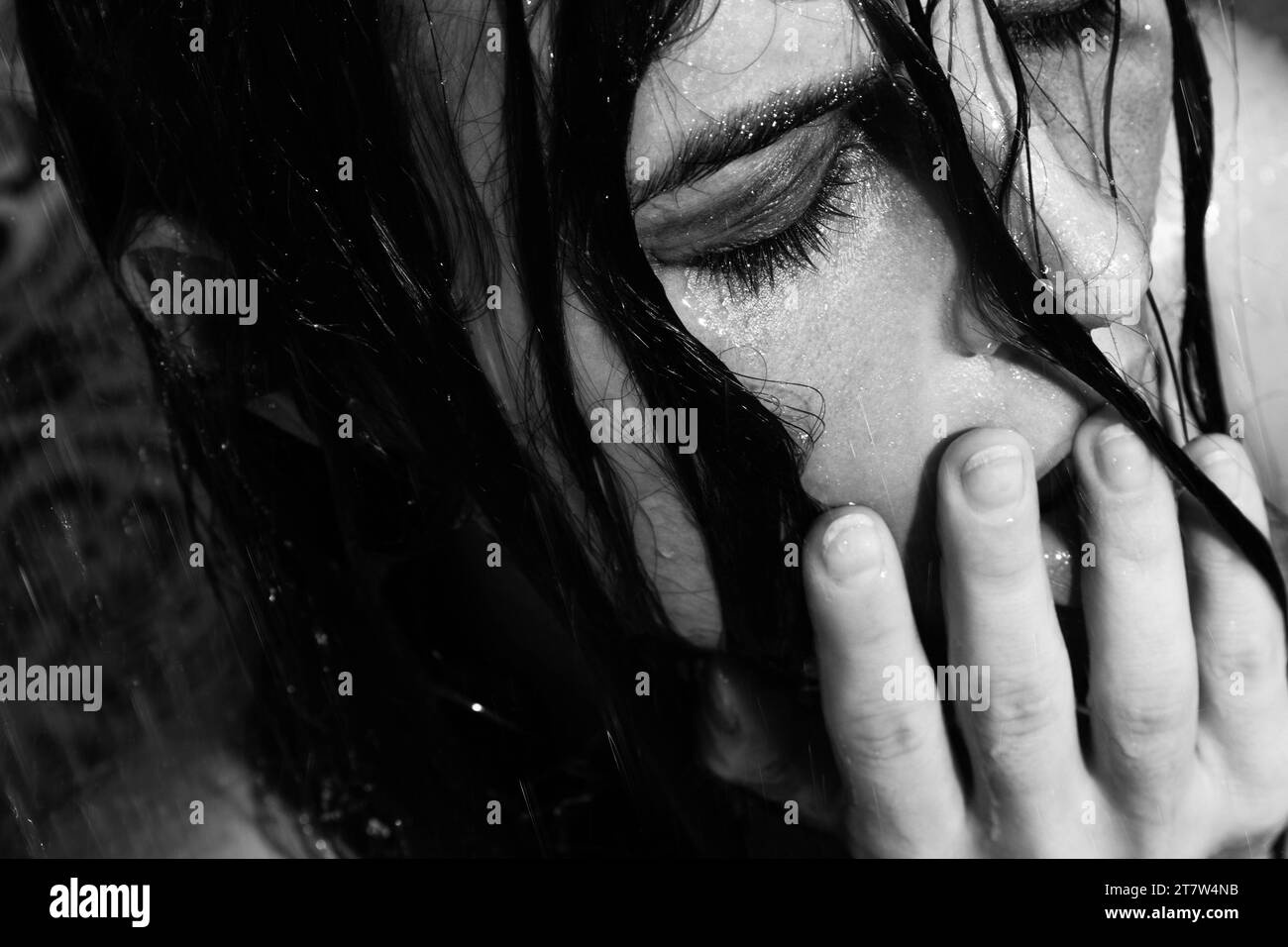 Sad and wet woman with smudged makeup on her face under the shower ...