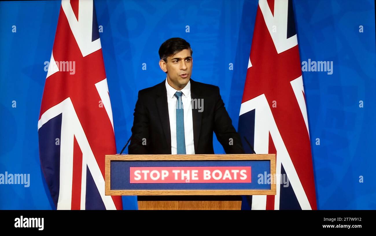 Prime Minister Rishi Sunak standing at podium with Stop the Boats sign flanked by Union Jack ...