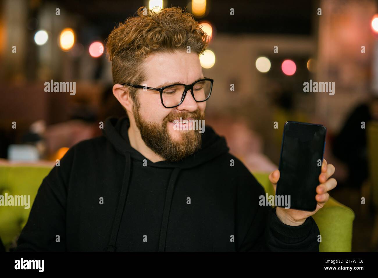Satisfied man with dark beard holding smartphone and showing his ...