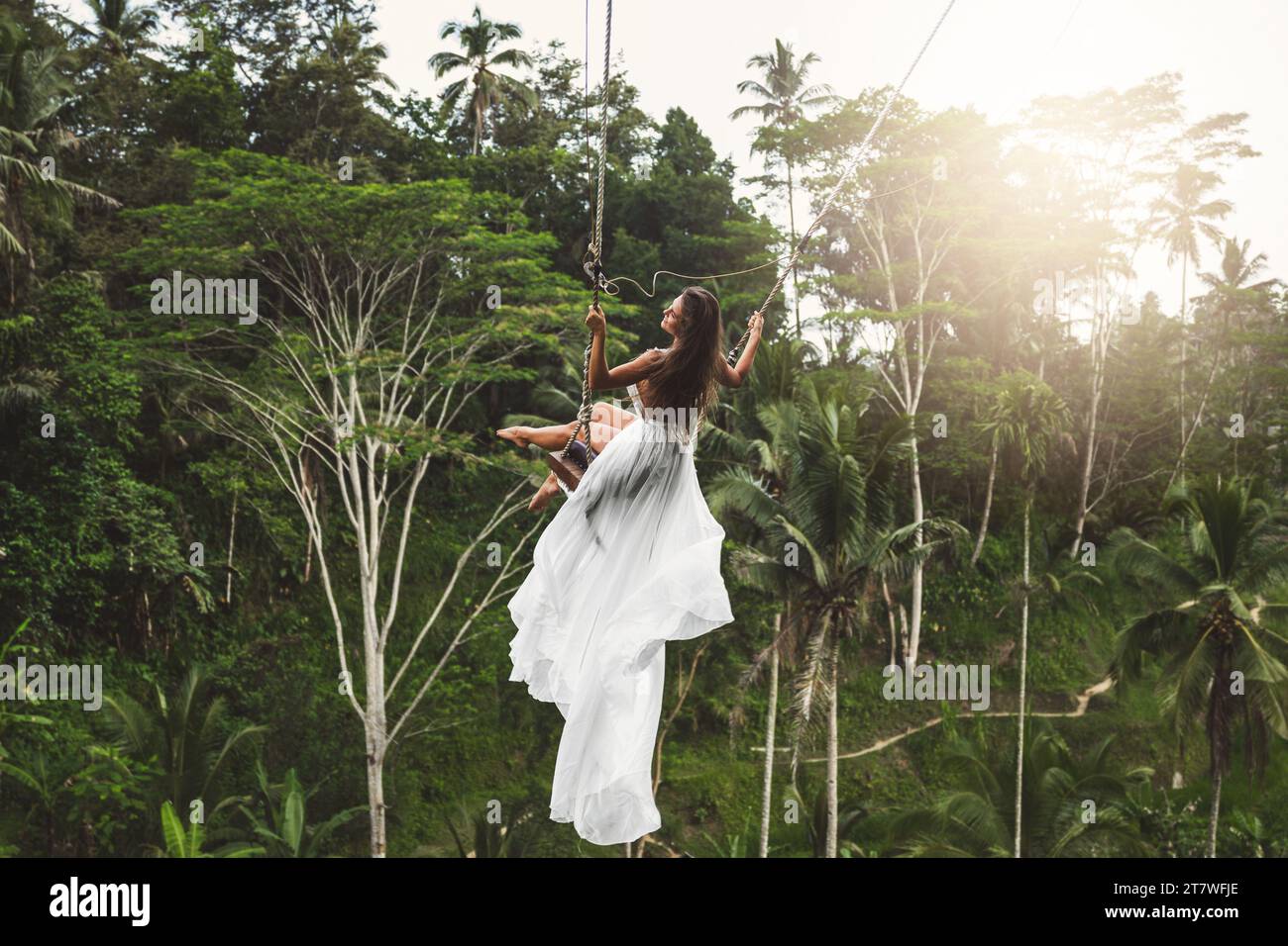 Woman wearing white dress swinging on rope swings with beautiful view ...