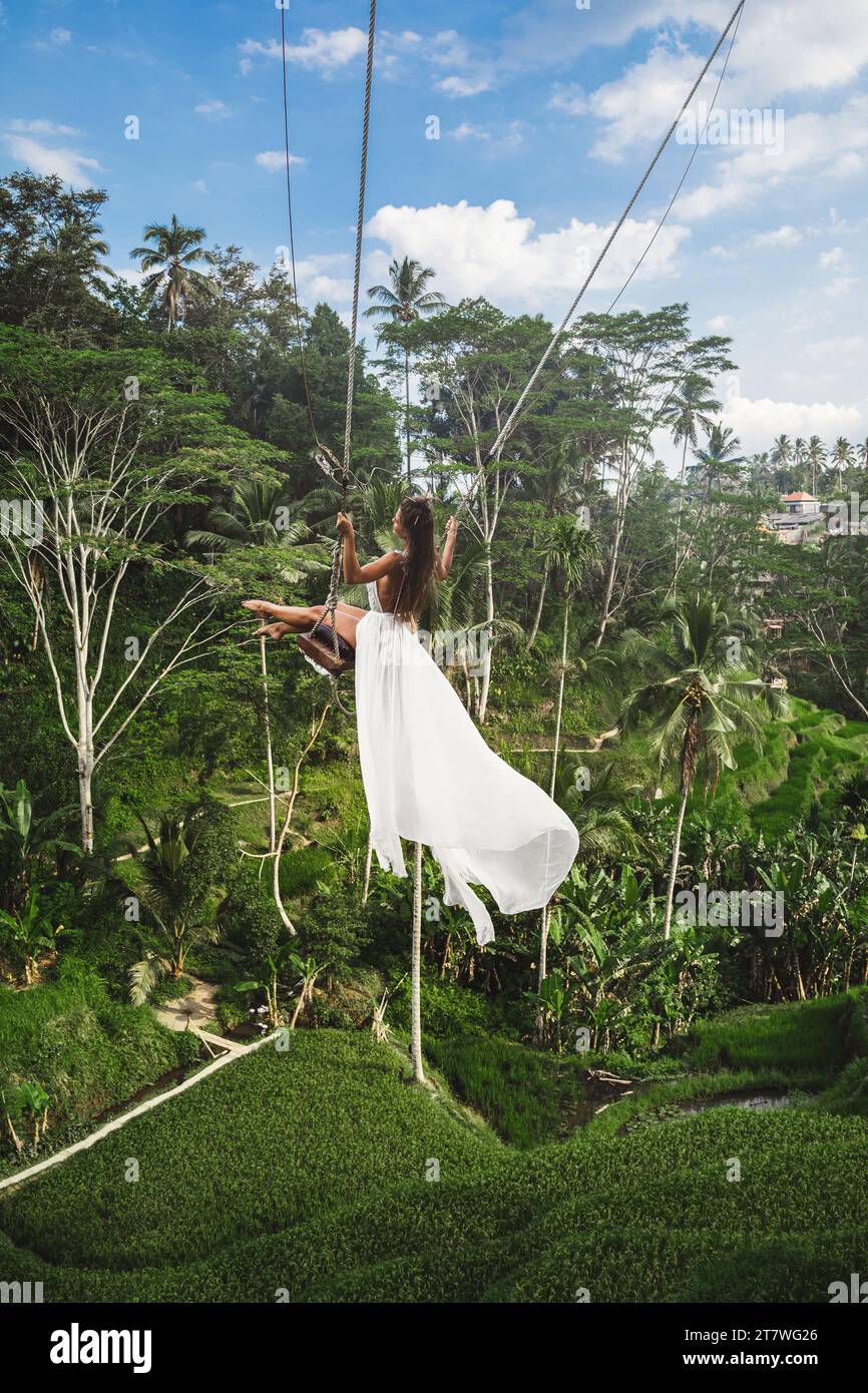 Woman wearing white dress swinging on rope swings with beautiful view ...