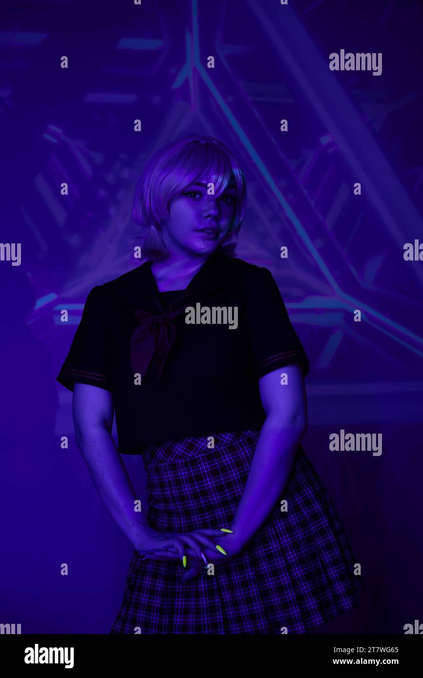 young blonde woman in school uniform in neon light on blue abstract ...