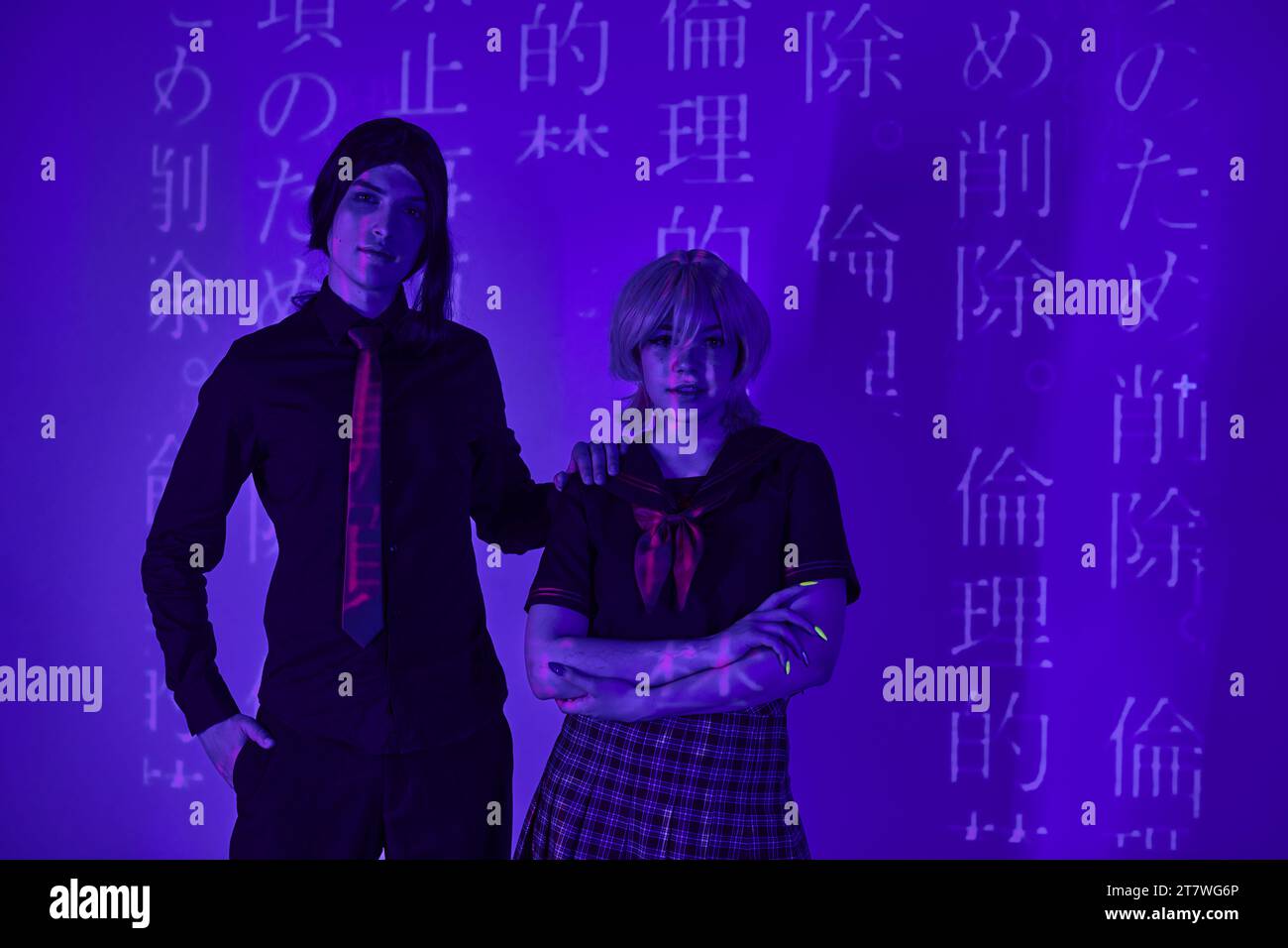 modern cosplayers in students uniform looking at camera in vibrant blue ...