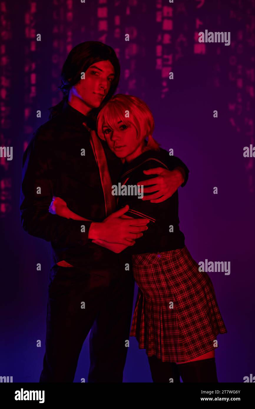 students in wigs and uniform embracing in red neon light on purple ...