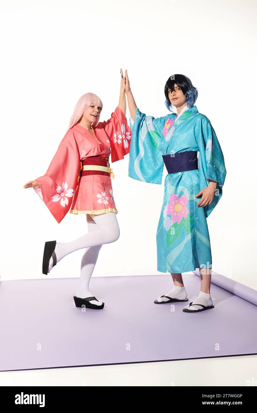 happy cosplayers in bright kimono and wigs giving high five on purple ...