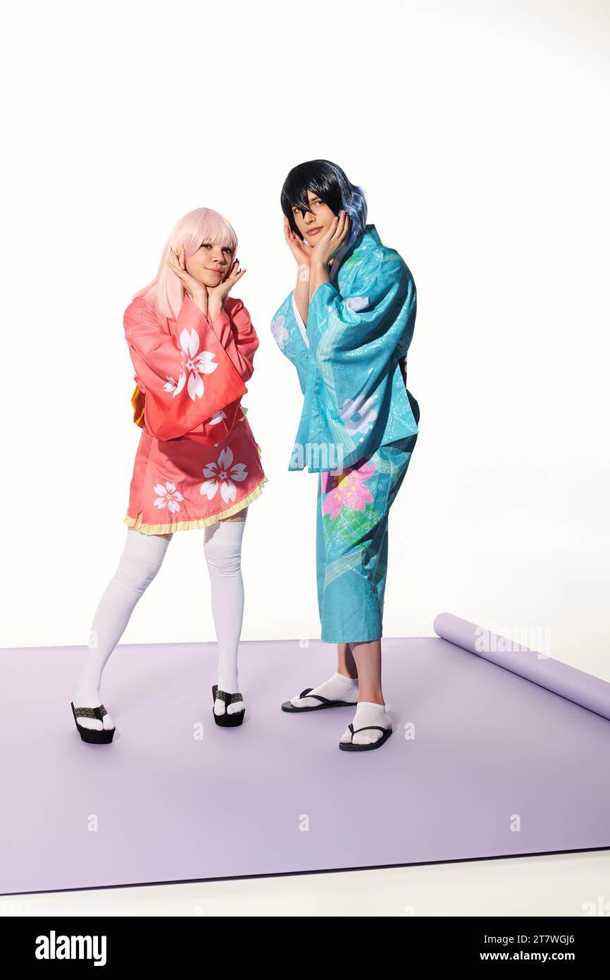 playful couple of cosplayers in vibrant outfit touching faces on purple ...