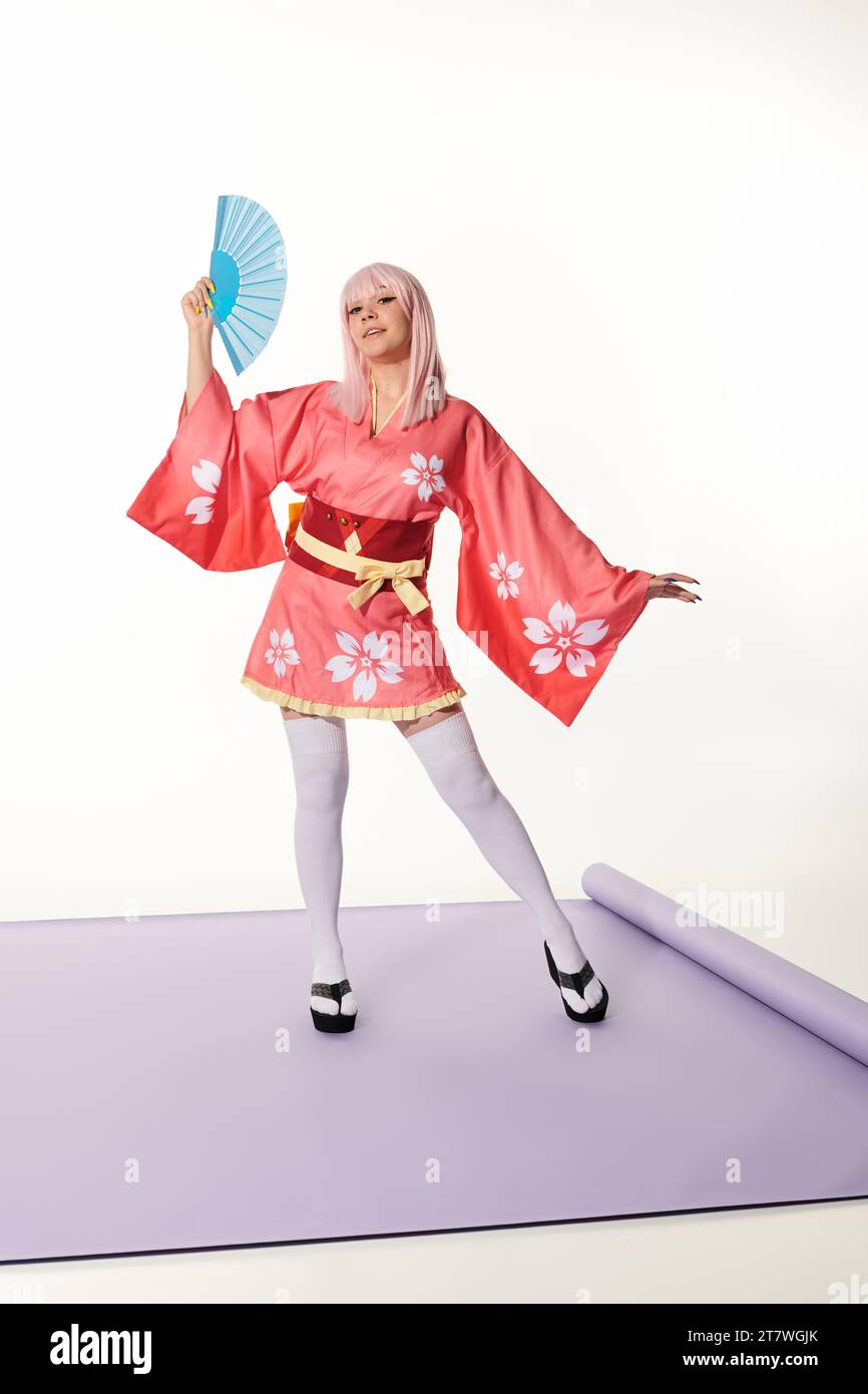 artistic cosplay woman in pink kimono and blonde wig with hand fan on ...