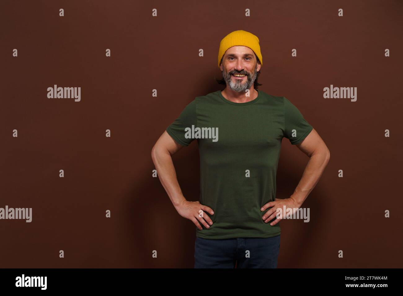 Happy confident middle-aged man standing with hands on sides on brown ...