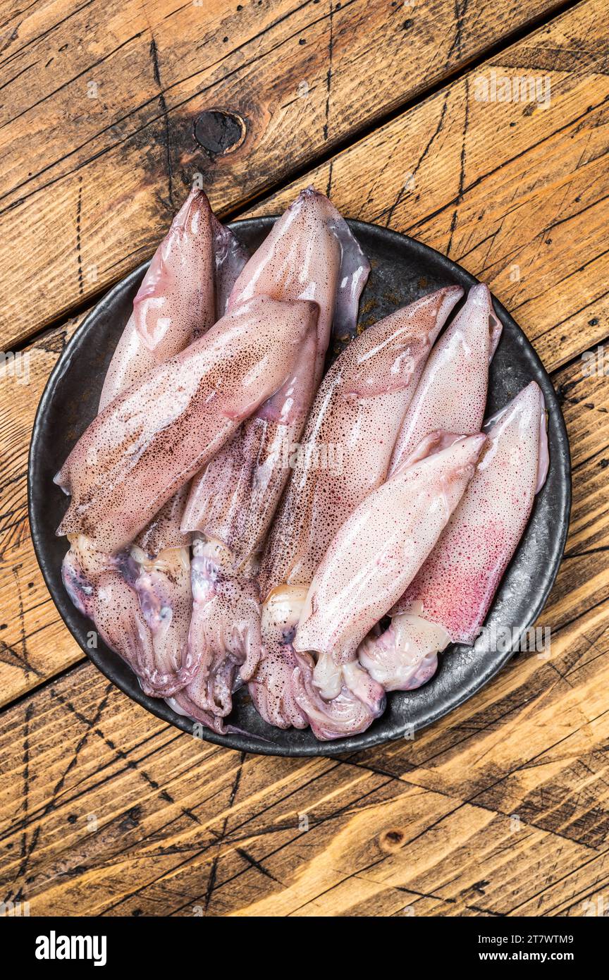Raw squid, fresh calamari in a plate. Wooden background. Top view Stock ...