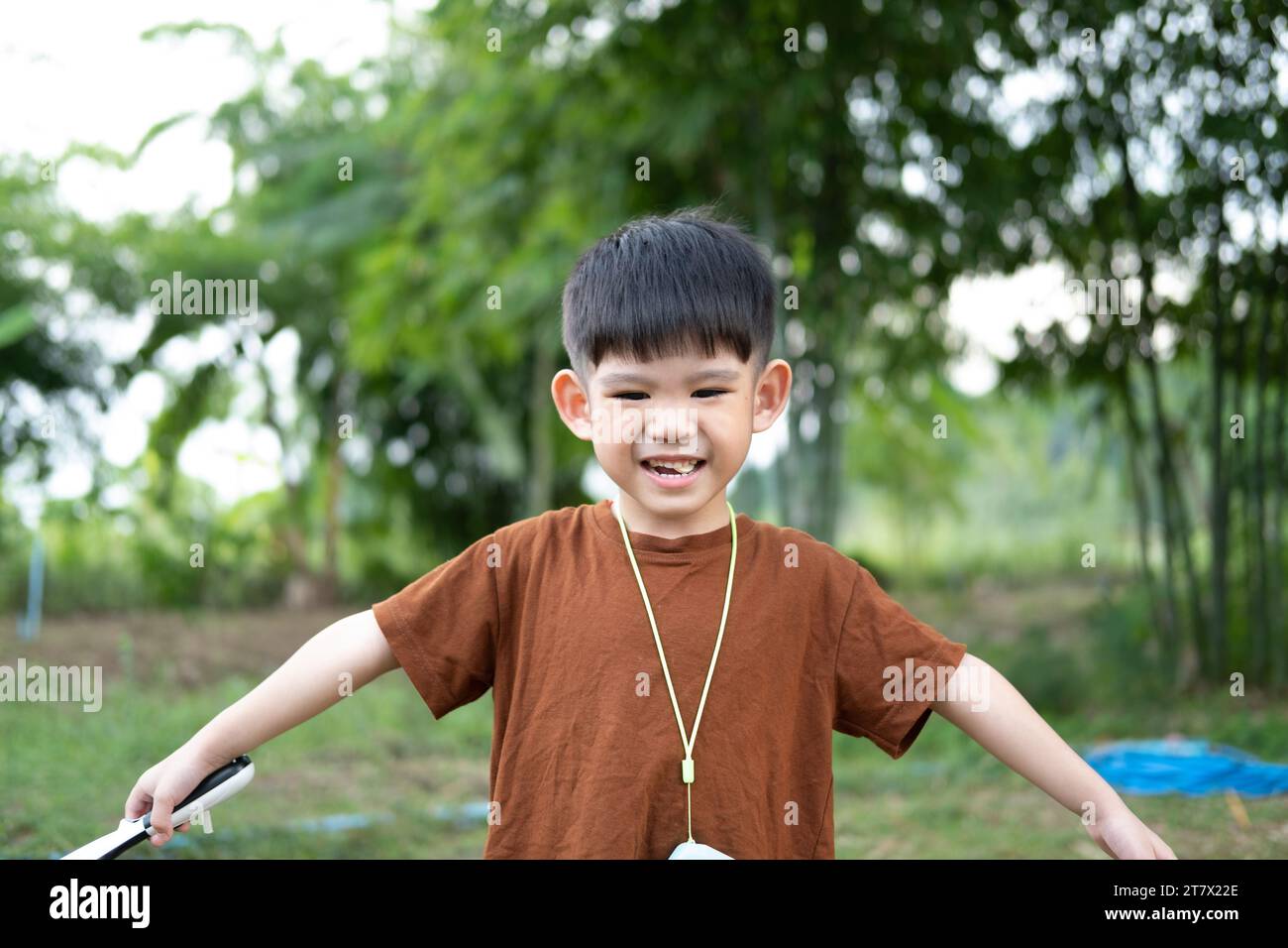 Asian boy standing with arms spread in a relaxed pose at outdoor area ...