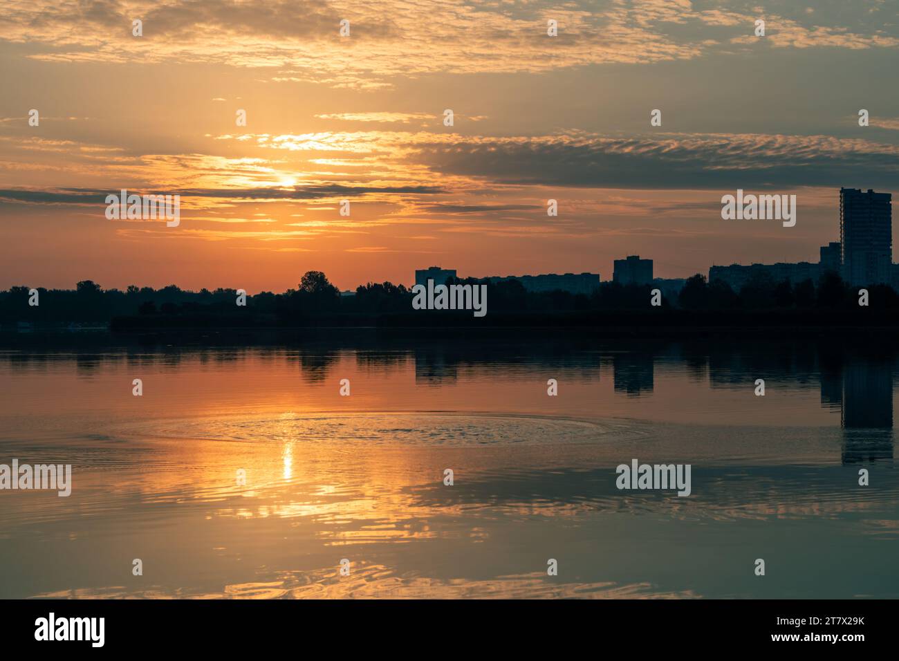 Scenic warm sunrise sun on cloudy sky reflecting in lake water ...