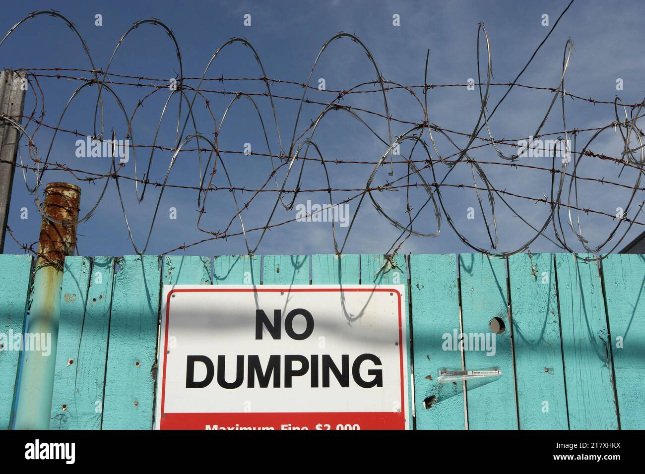 No dumping sign on fence with barbed wire and razor wire against blue ...