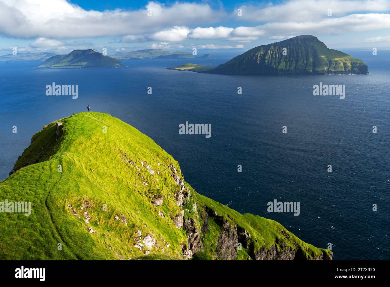 Hiker walks on top of a tall cliff overlooking the ocean, Nordradalur ...