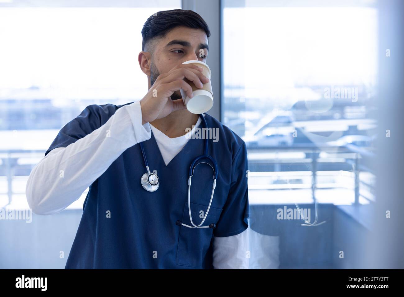 Biracial male doctor drinking coffee in sunny hospital office Stock ...