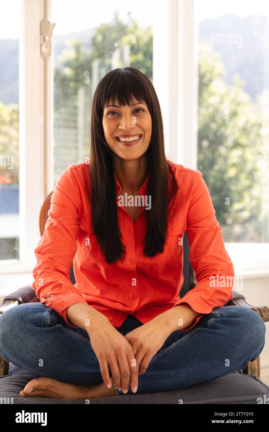 Happy biracial woman having video call sitting cross legged smiling in sunny room Stock Photo ...