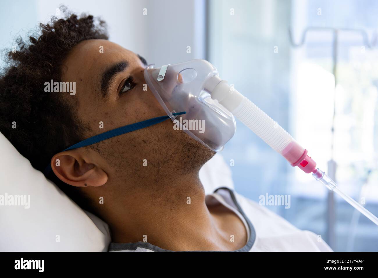 Biracial male patient with oxygen mask lying in bed in sunny hospital ...