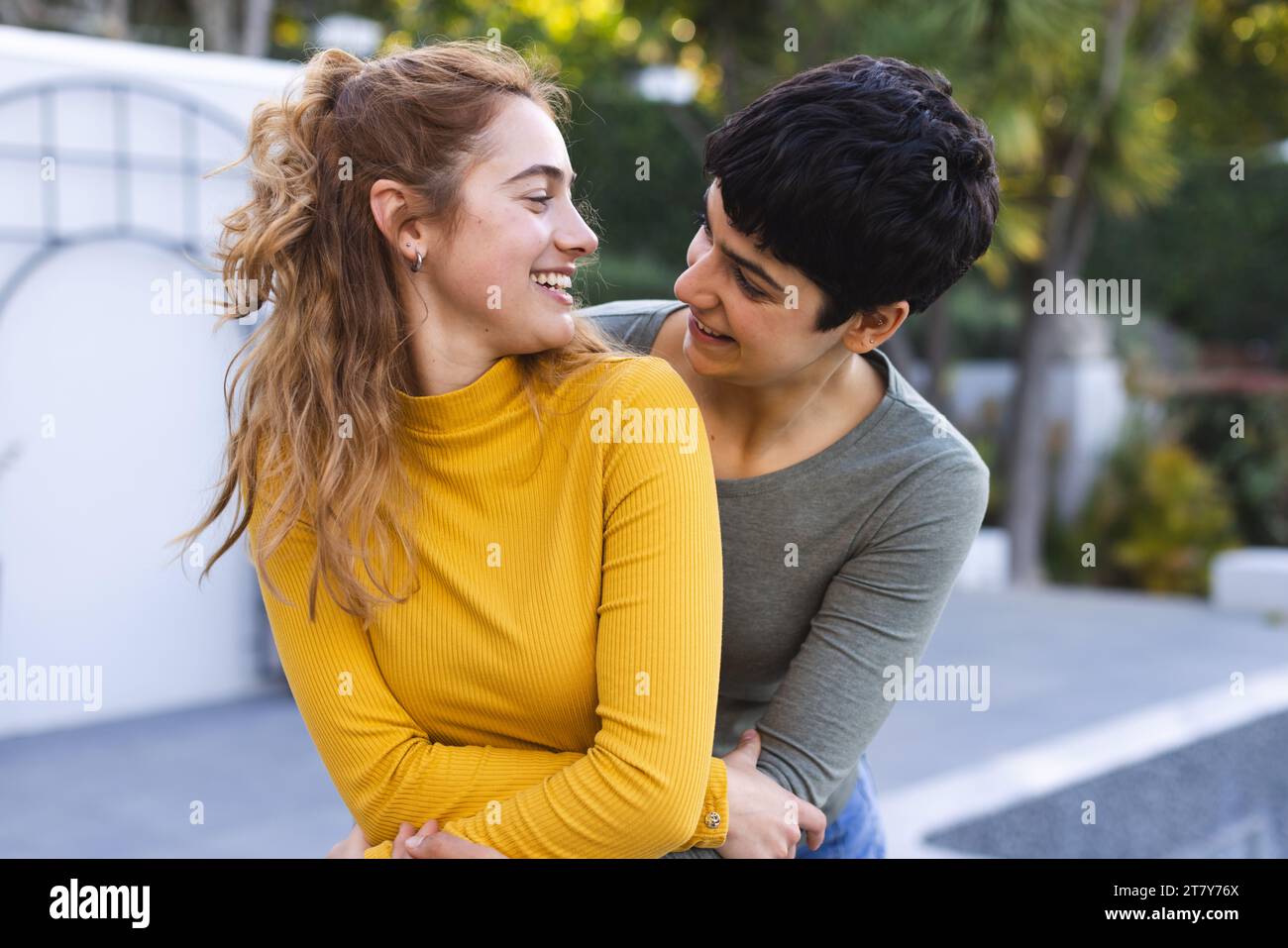 Happy Biracial Lesbian Couple Standing On Garden Terrace Embracing And