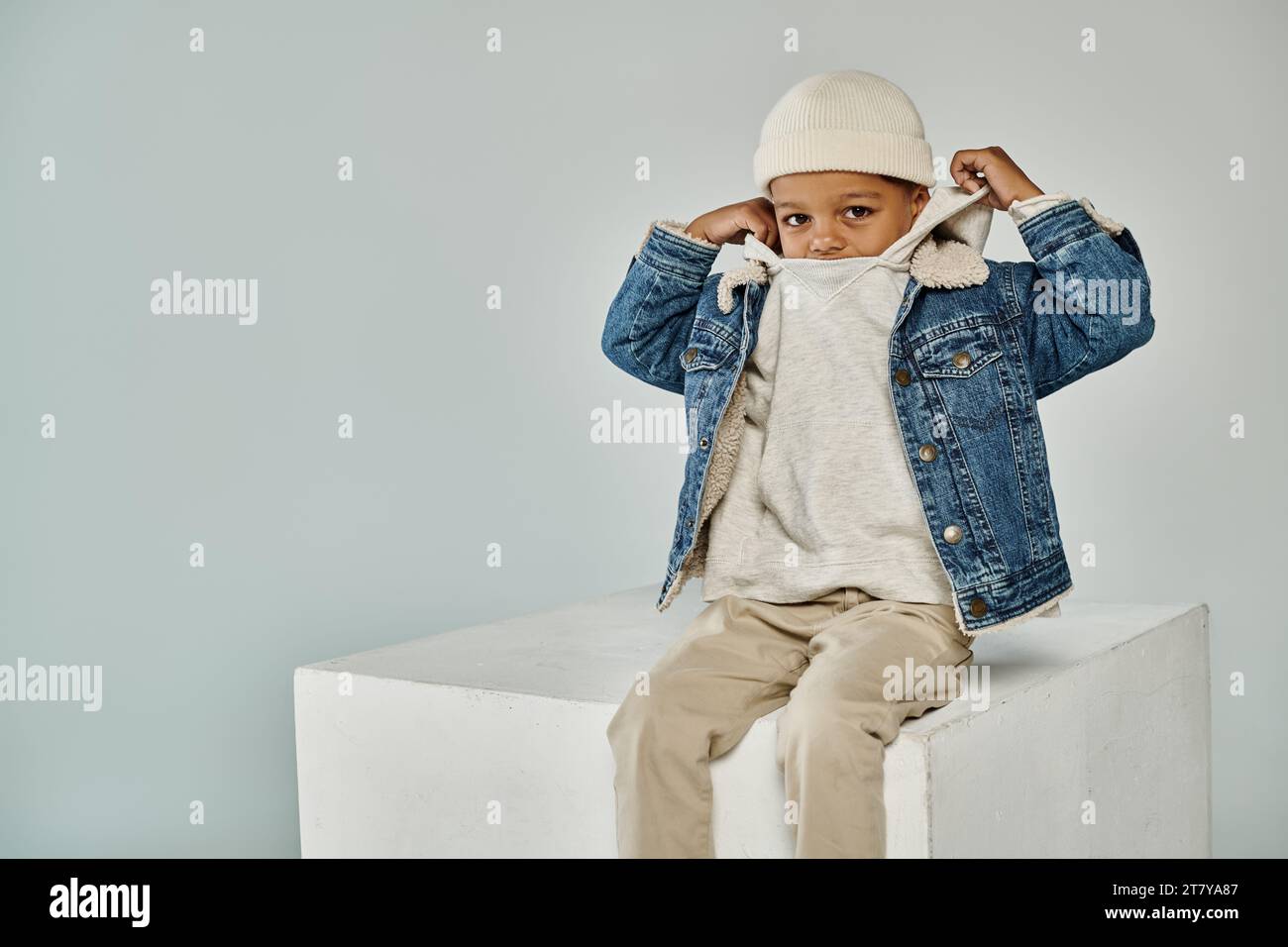 cute african american boy in winter attire and beanie sitting on ...