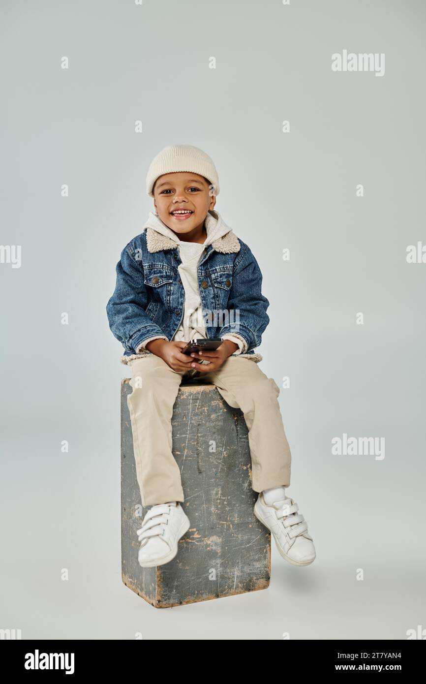 happy african american boy in winter attire and beanie using smartphone ...
