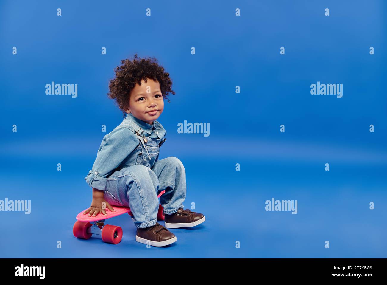 adorable african american toddler boy in denim clothes sitting on penny ...