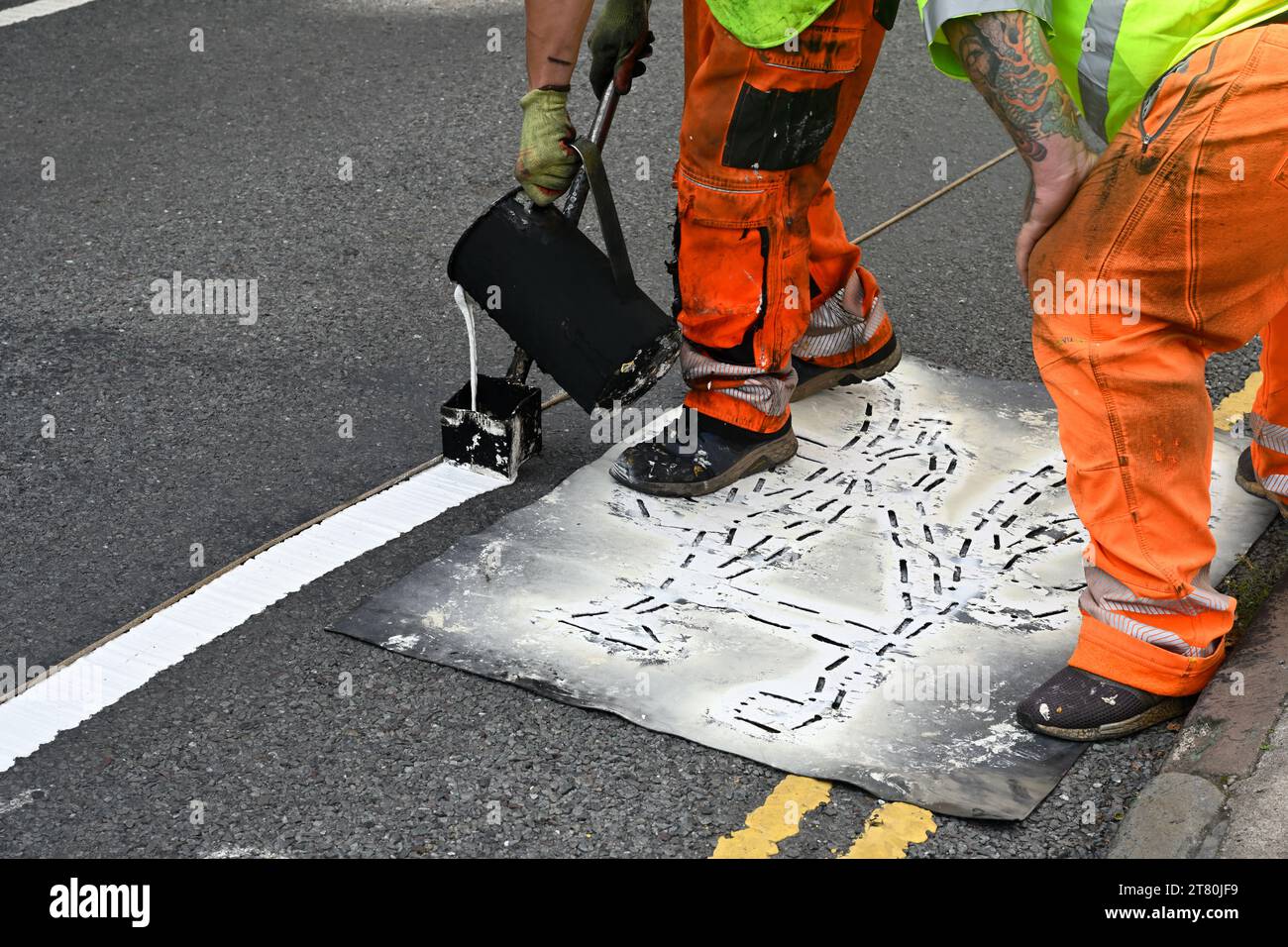 Workman painting white line with hot molten paint and laying stencil for cycle lane, Bristol, UK ...