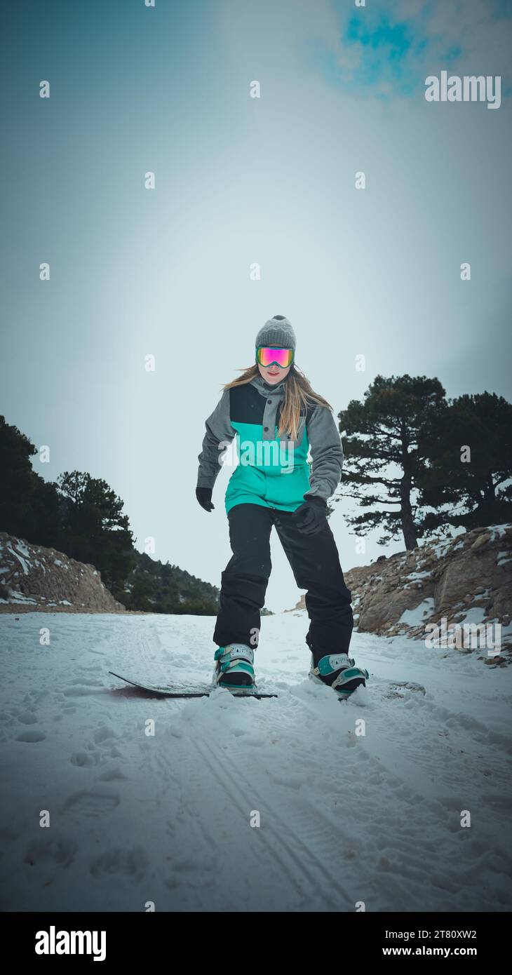 A female snowboarder in a ready stance on the top of a hill, as she ...