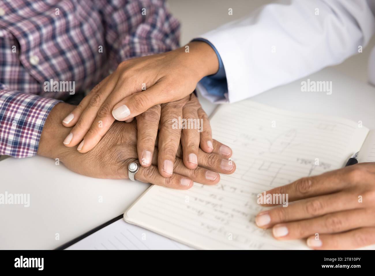 Younger doctor woman touching stacked hands of senior male patient ...