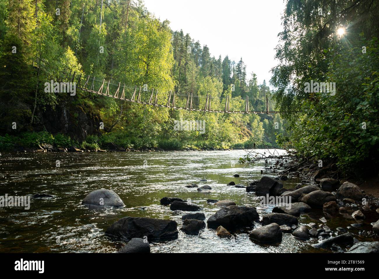 A suspension bridge over a fast flowing river in the forest in northern ...