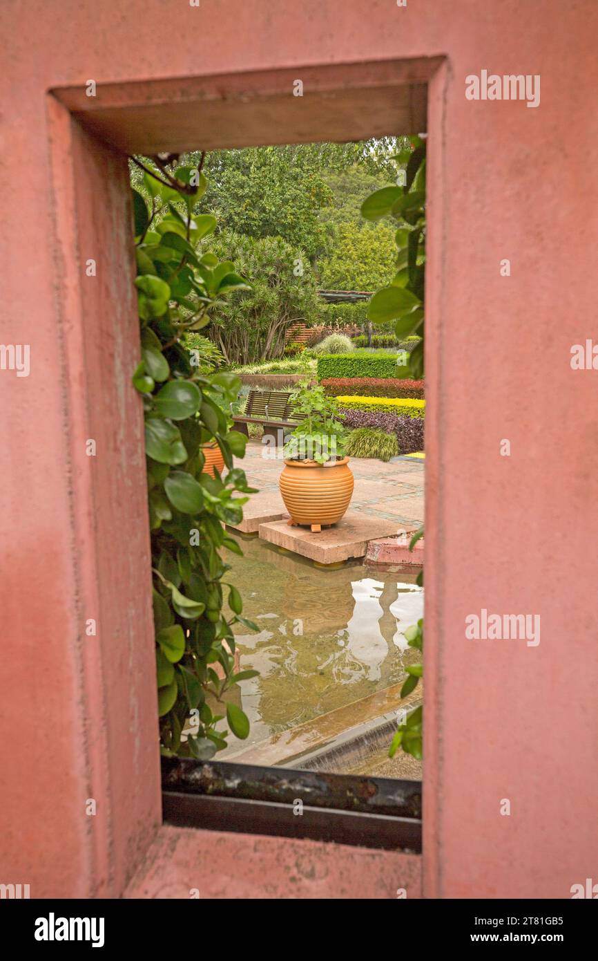 Window through thick wall framing garden with water feature, large pot ...