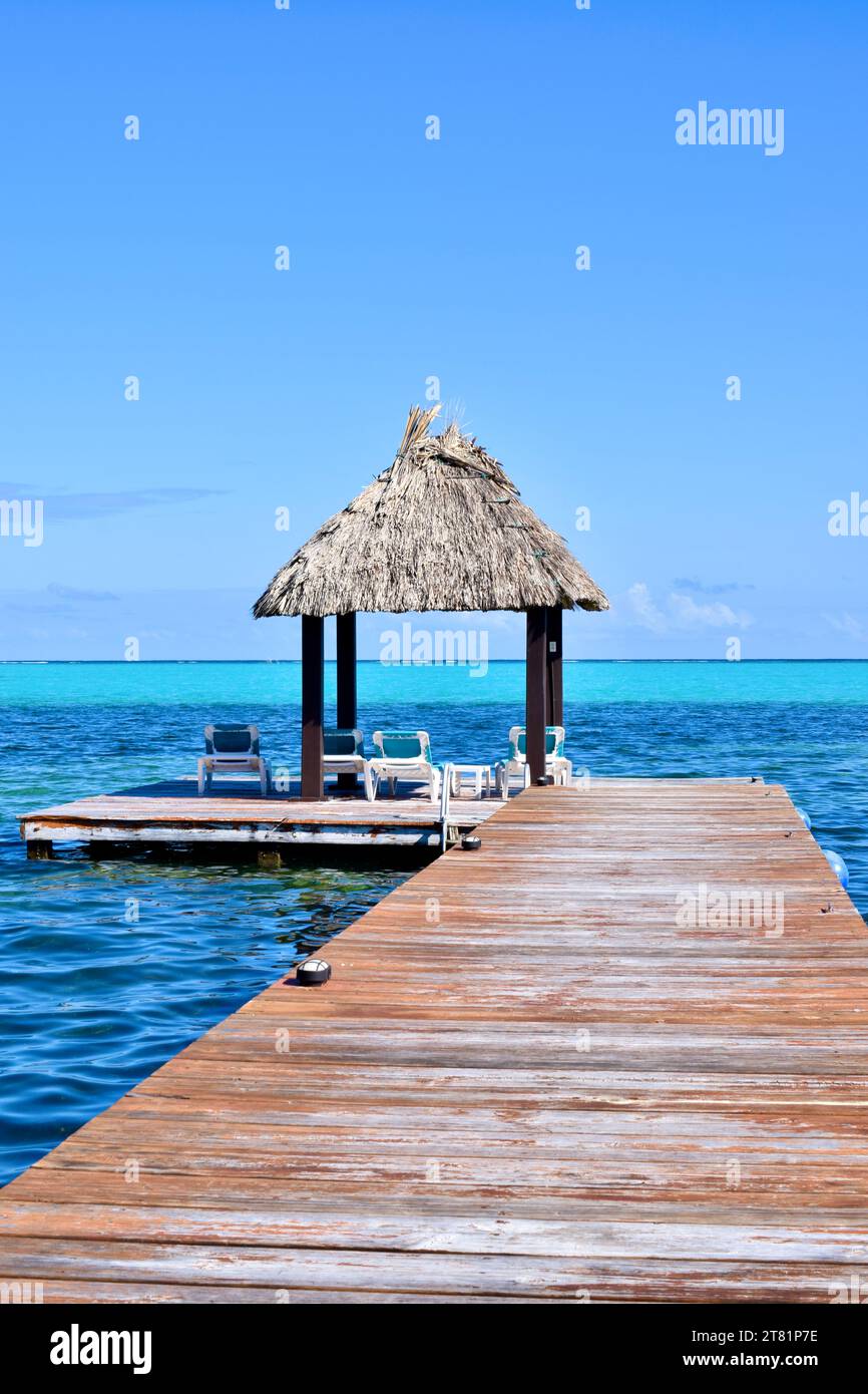 A pier and lounge chairs under a palapa facing the turquoise-blue ...