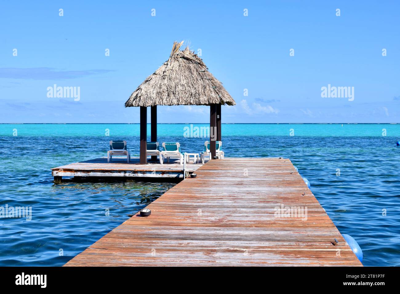 A pier and lounge chairs under a palapa facing the turquoise-blue ...