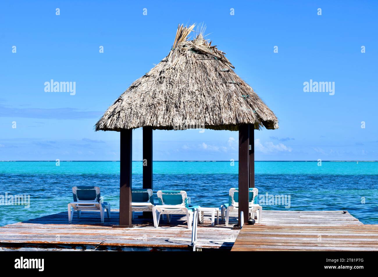 A pier and lounge chairs under a palapa facing the turquoise-blue ...