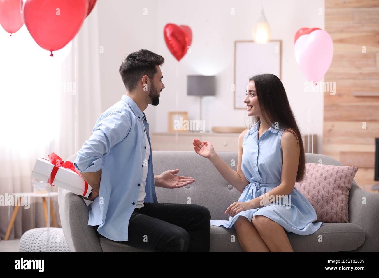 Young man presenting gift to his girlfriend in living room decorated ...