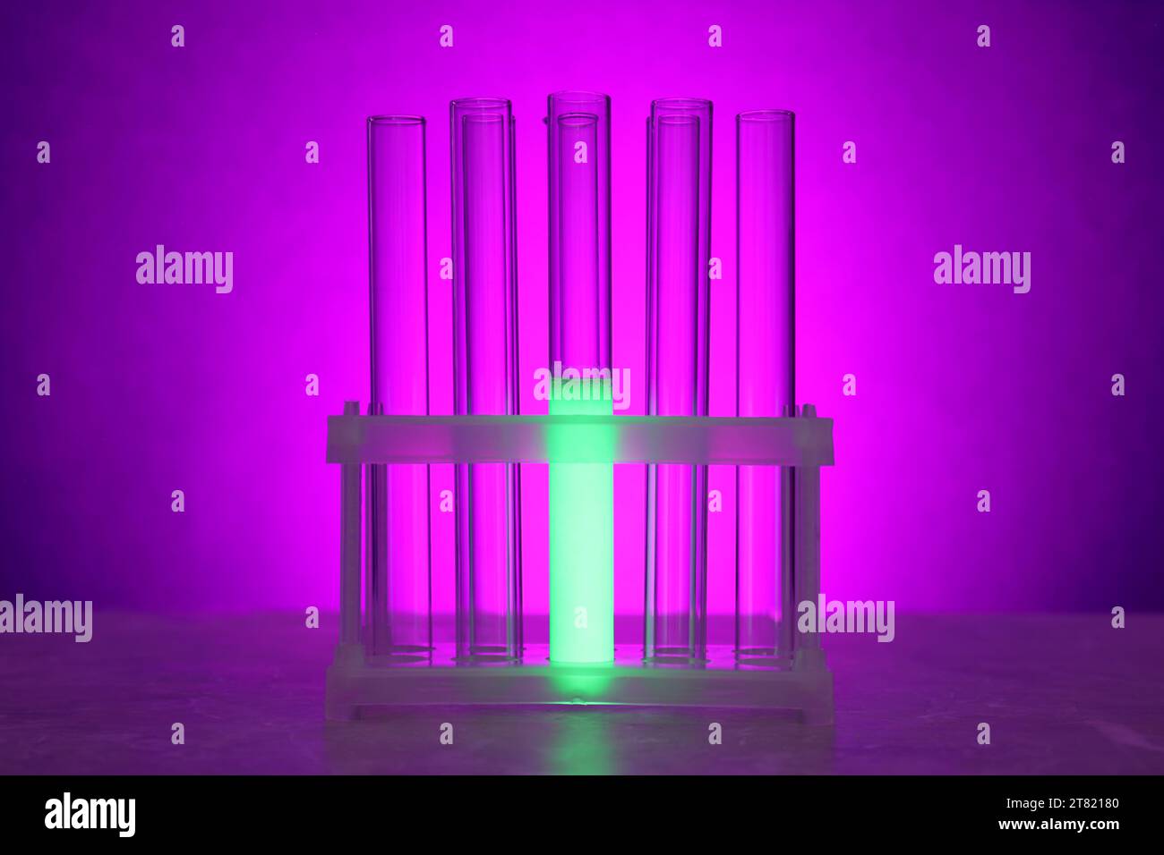 Test tube with luminous liquid on table against violet background Stock ...