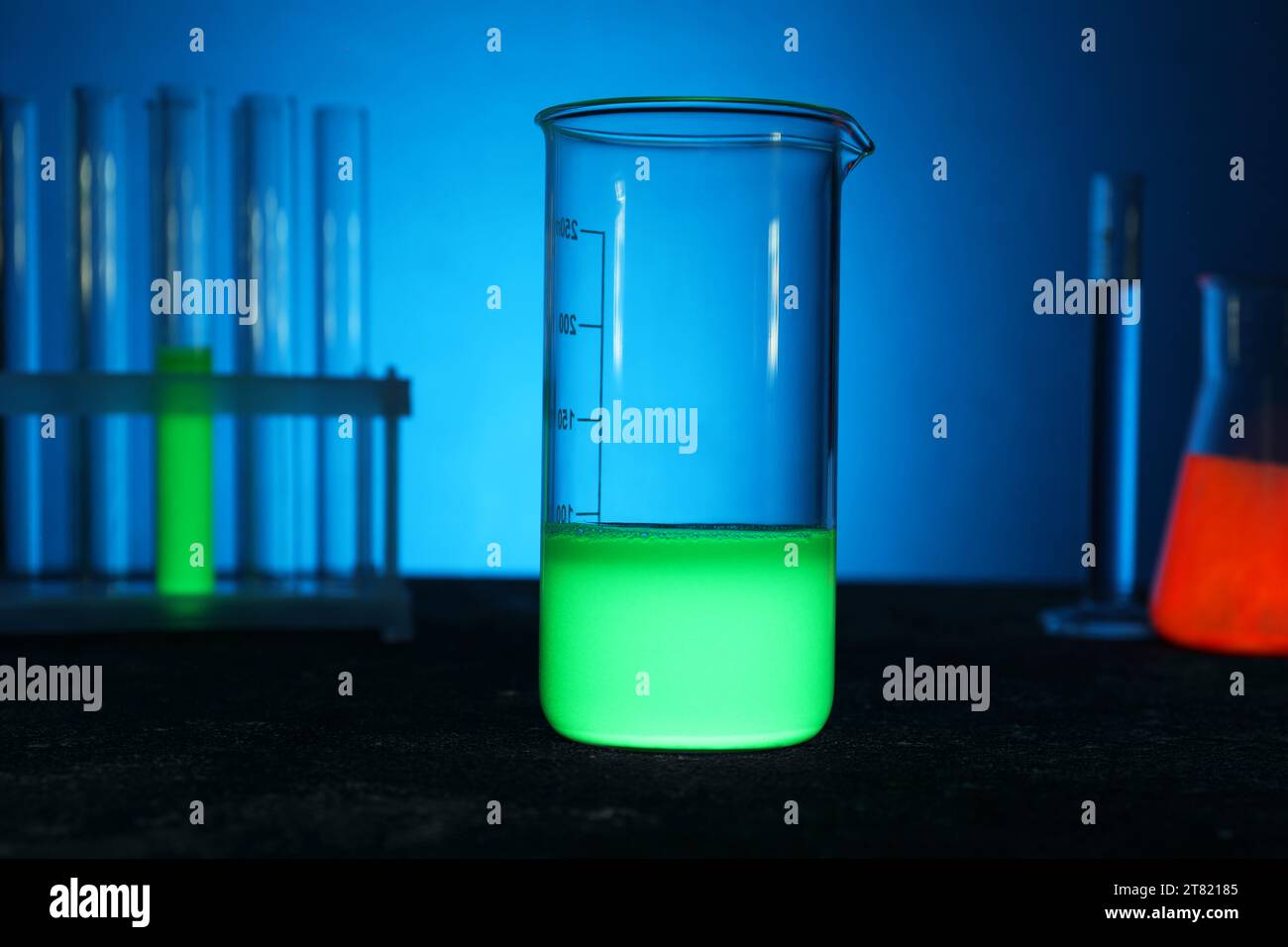 Laboratory beaker with luminous liquid on table against blue background ...