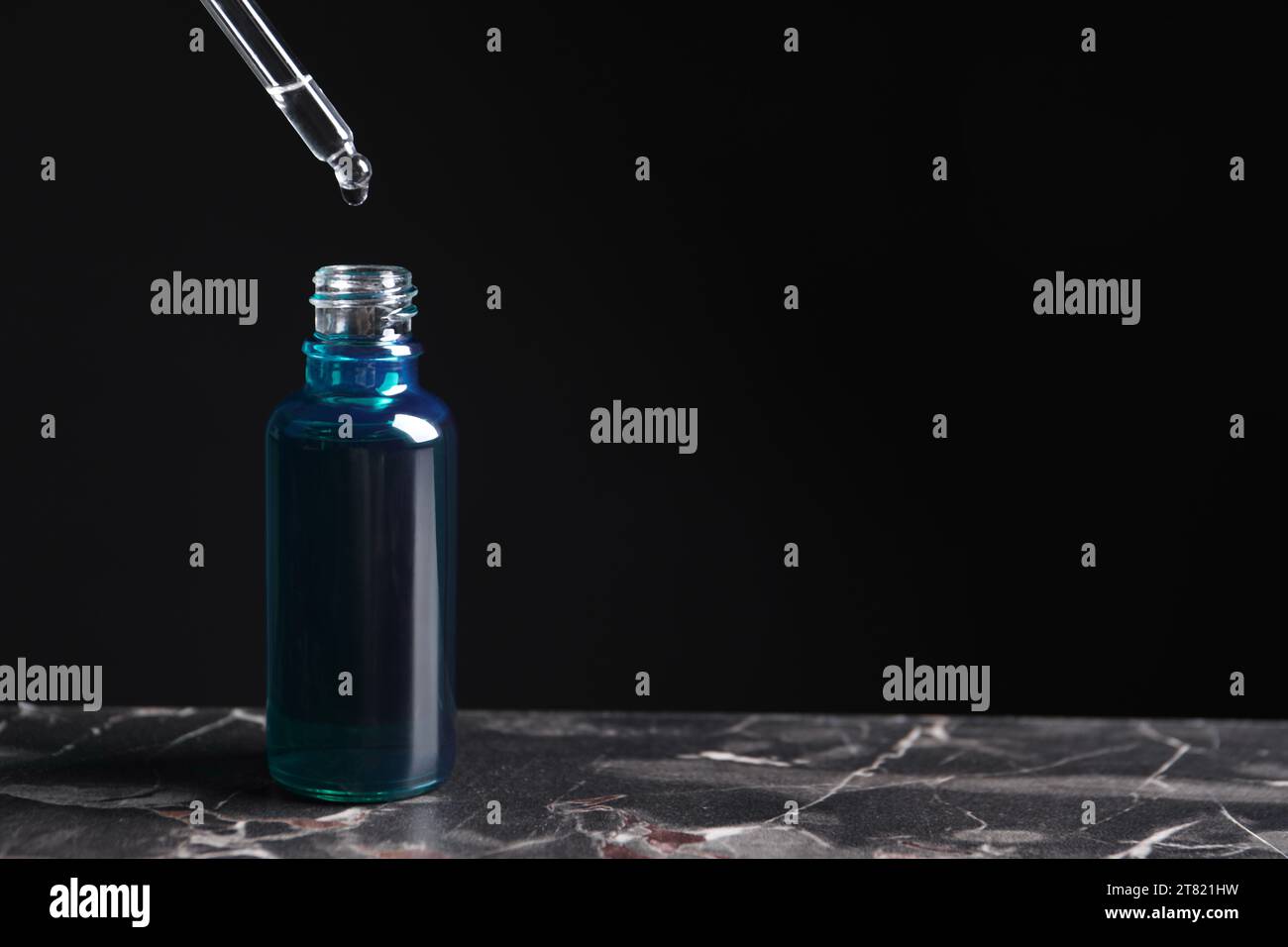 Dripping cosmetic serum from pipette into bottle on grey marble table ...