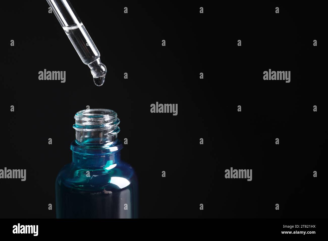Dripping cosmetic serum from pipette into bottle on black background ...