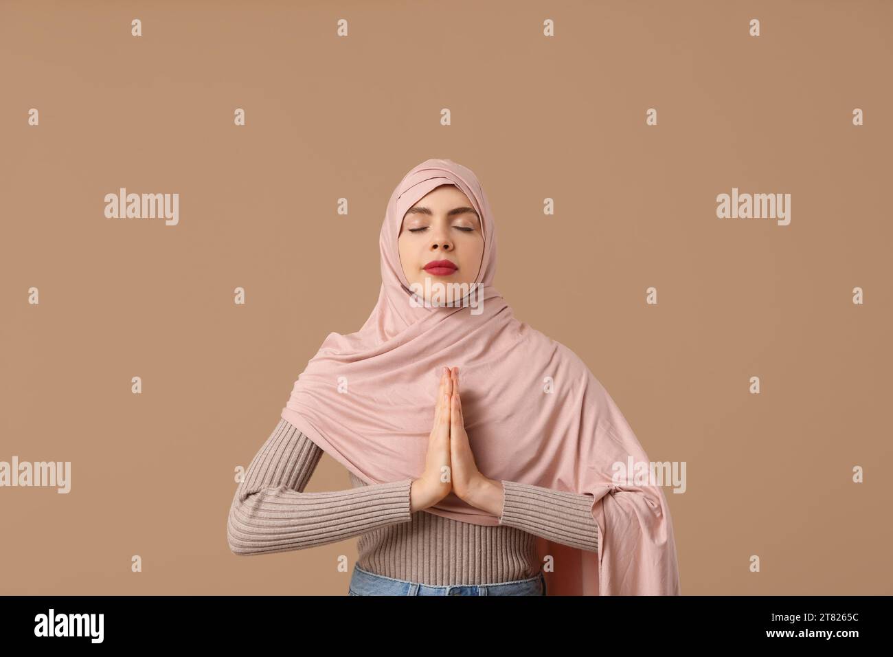 Beautiful young Muslim woman in hijab meditating on brown background ...
