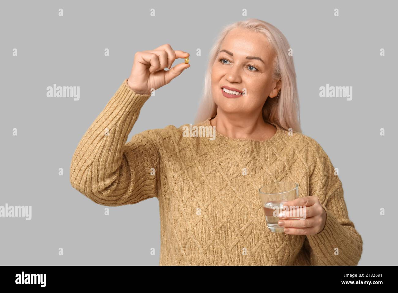 Beautiful mature woman with pill and glass of water on grey background ...