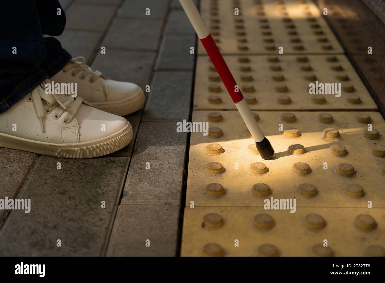 A close-up of a woman's feet with a tactile cane and a tactile tile ...