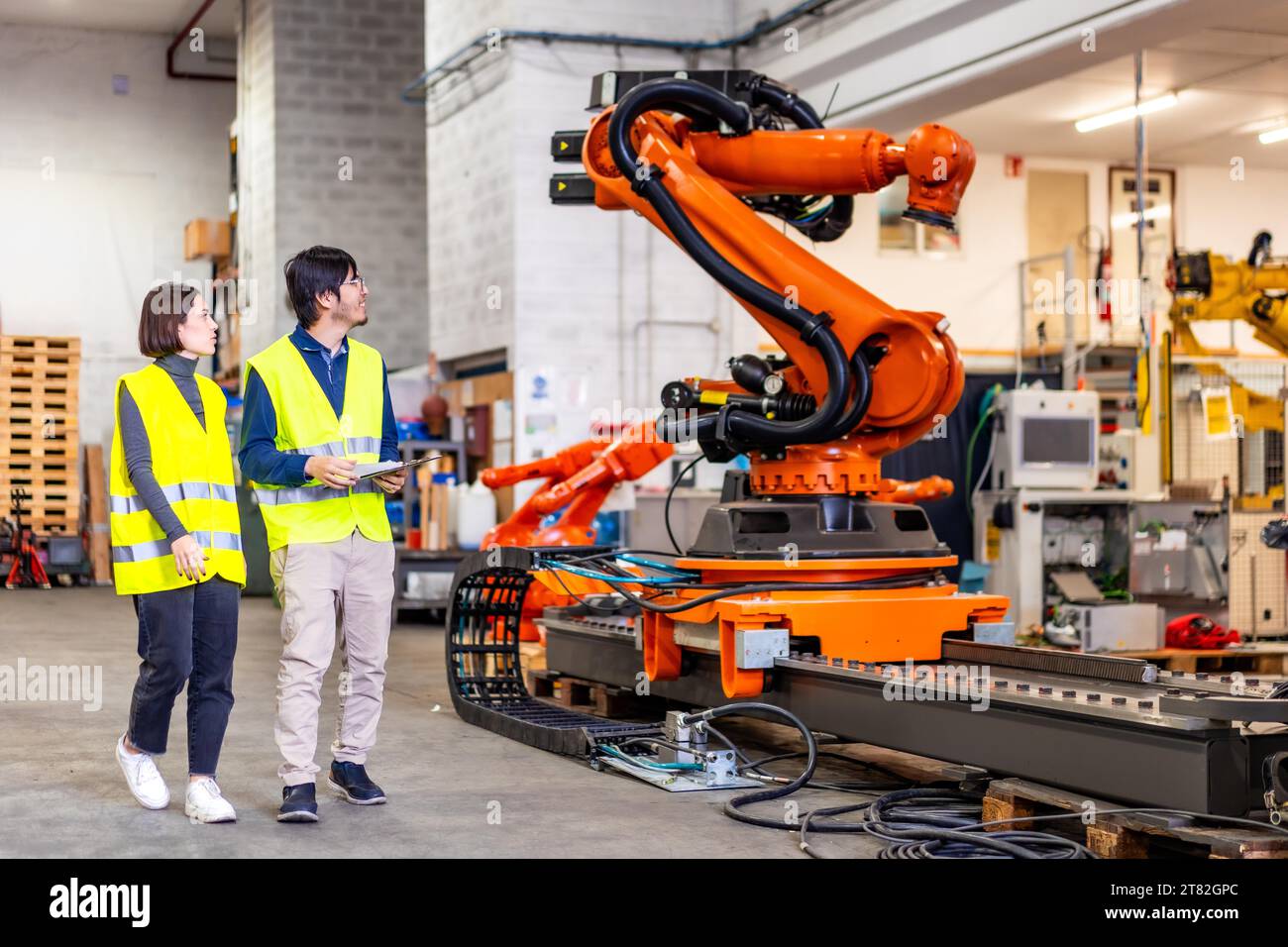 Two multi-ethnic engineers walking into the factory of robotic arms production Stock Photo - Alamy