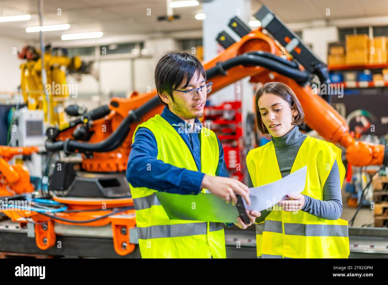 Multicultural engineers doing paperwork in an assembly line of robotic ...