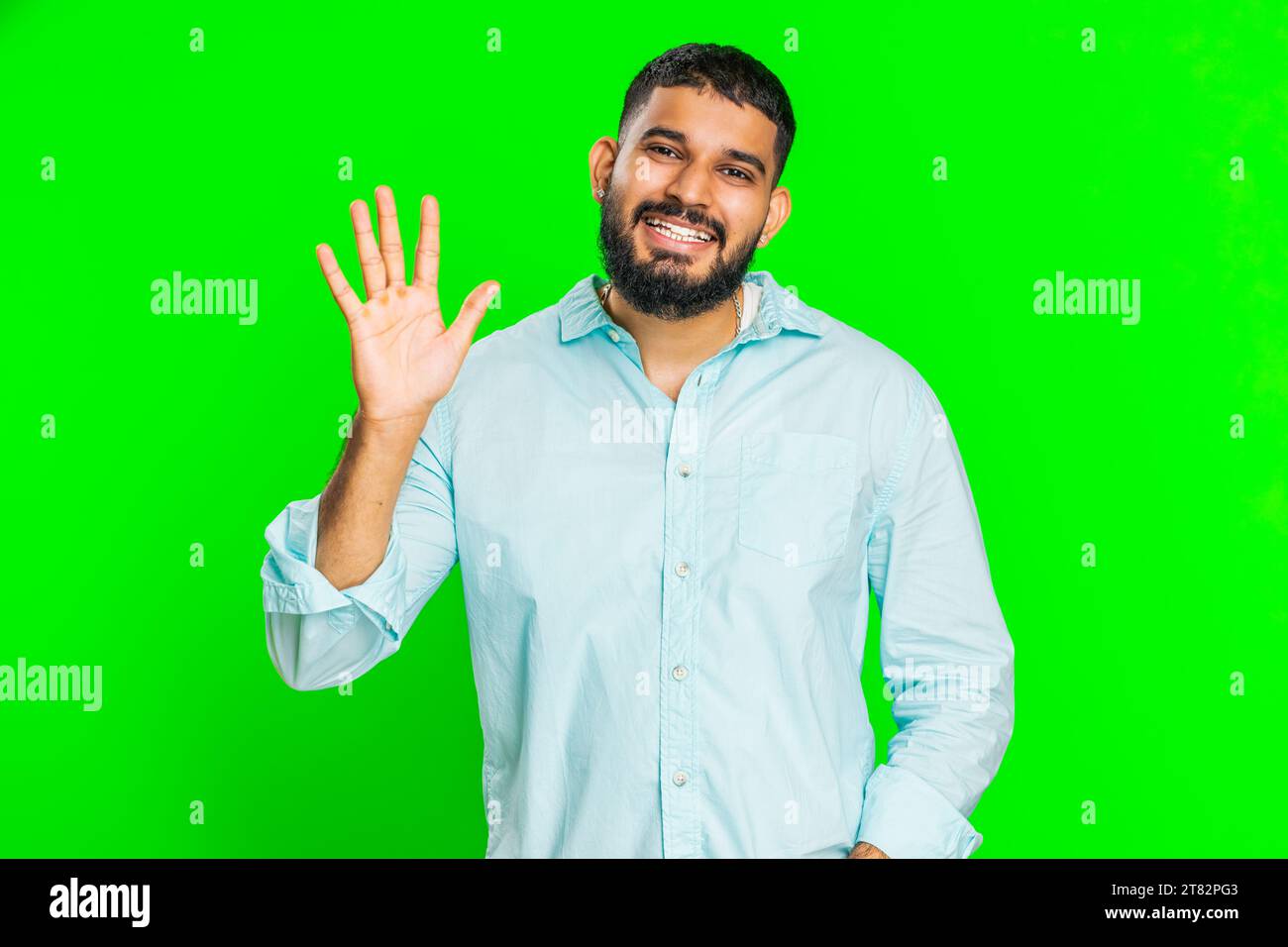 Young Indian man smiling friendly at camera, waving hands gesturing ...