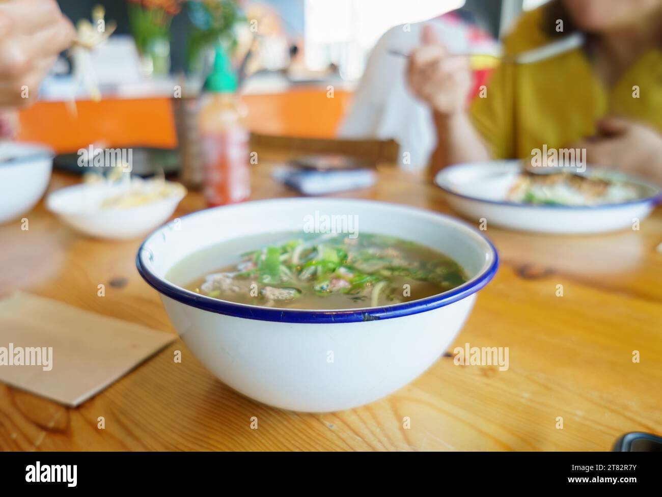 Vietnamese Pho dish in a white bowl. Unrecognizable people enjoying ...