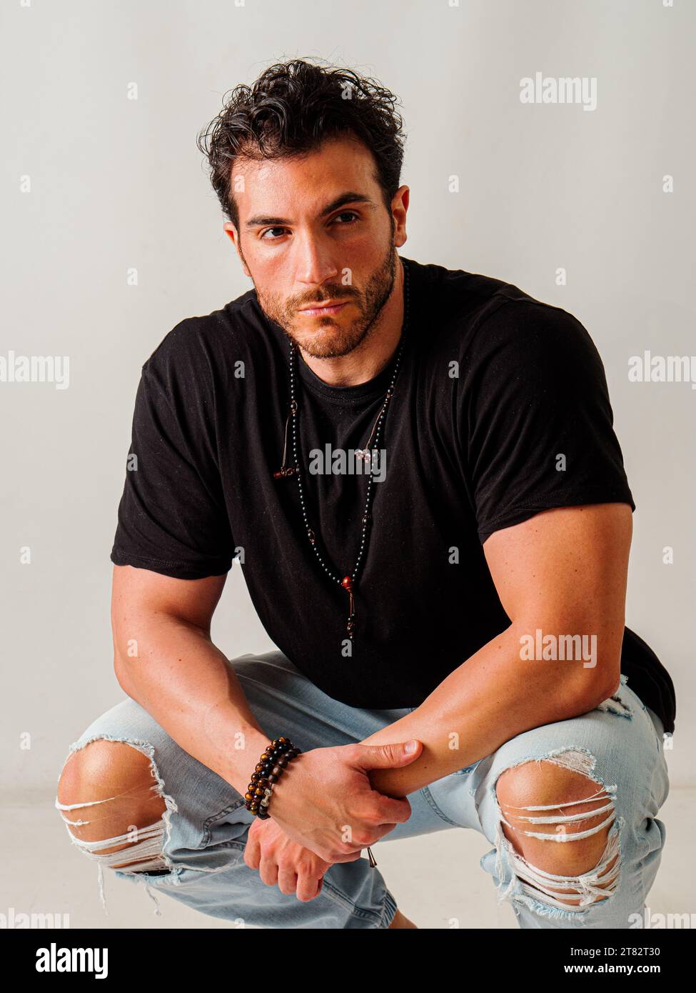 A man crouching on the ground wearing ripped jeans, in studio, on white ...