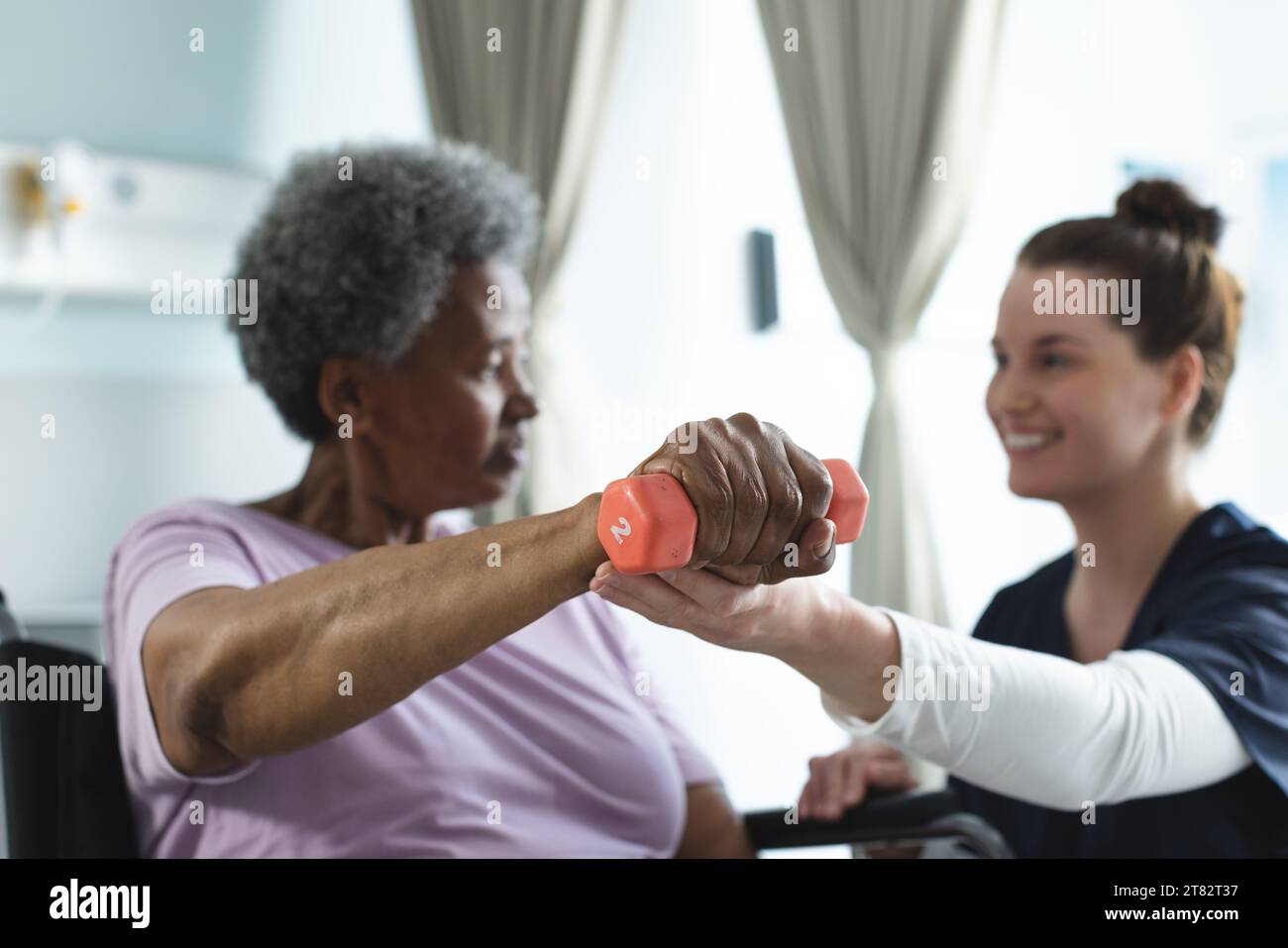 Diverse senior female patient exercising with weight and female doctor ...